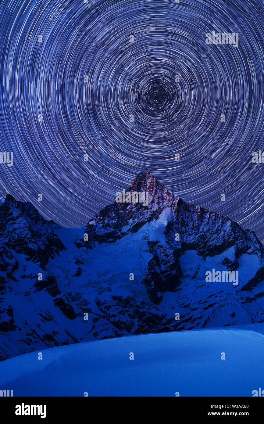 Incredible night view in Swiss Alps. Star trails moving in blue sky ...