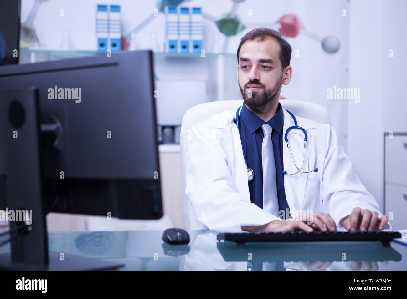 Portrait of doctor working on his computer in cabinet at the hospital ...