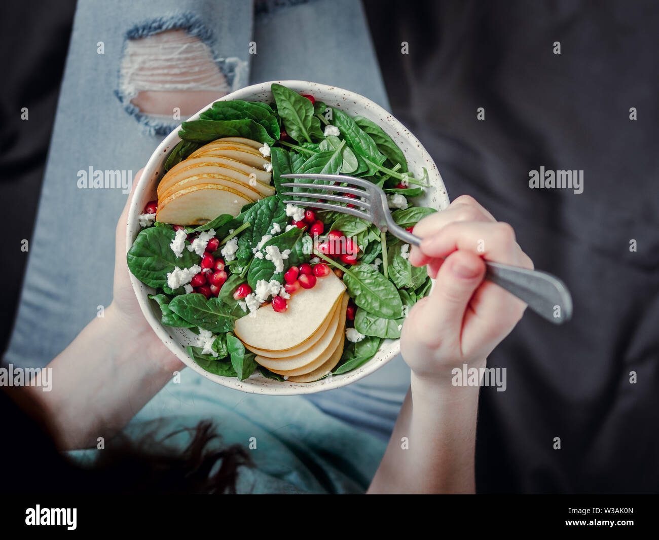 Woman in jeans holding vegan salad bowl with spinach, pear, pomegranate ...