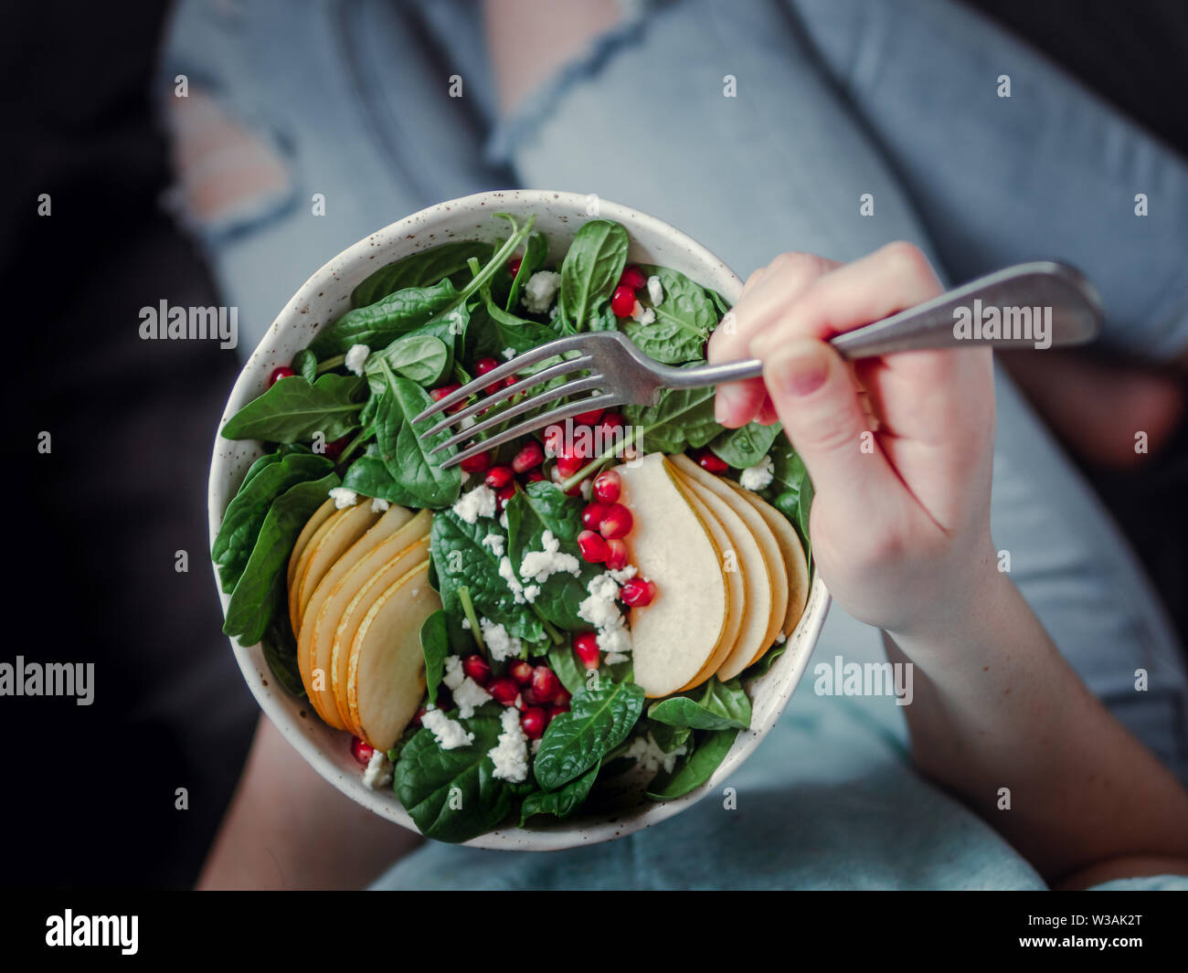 Woman in jeans holding vegan salad bowl with spinach, pear, pomegranate ...