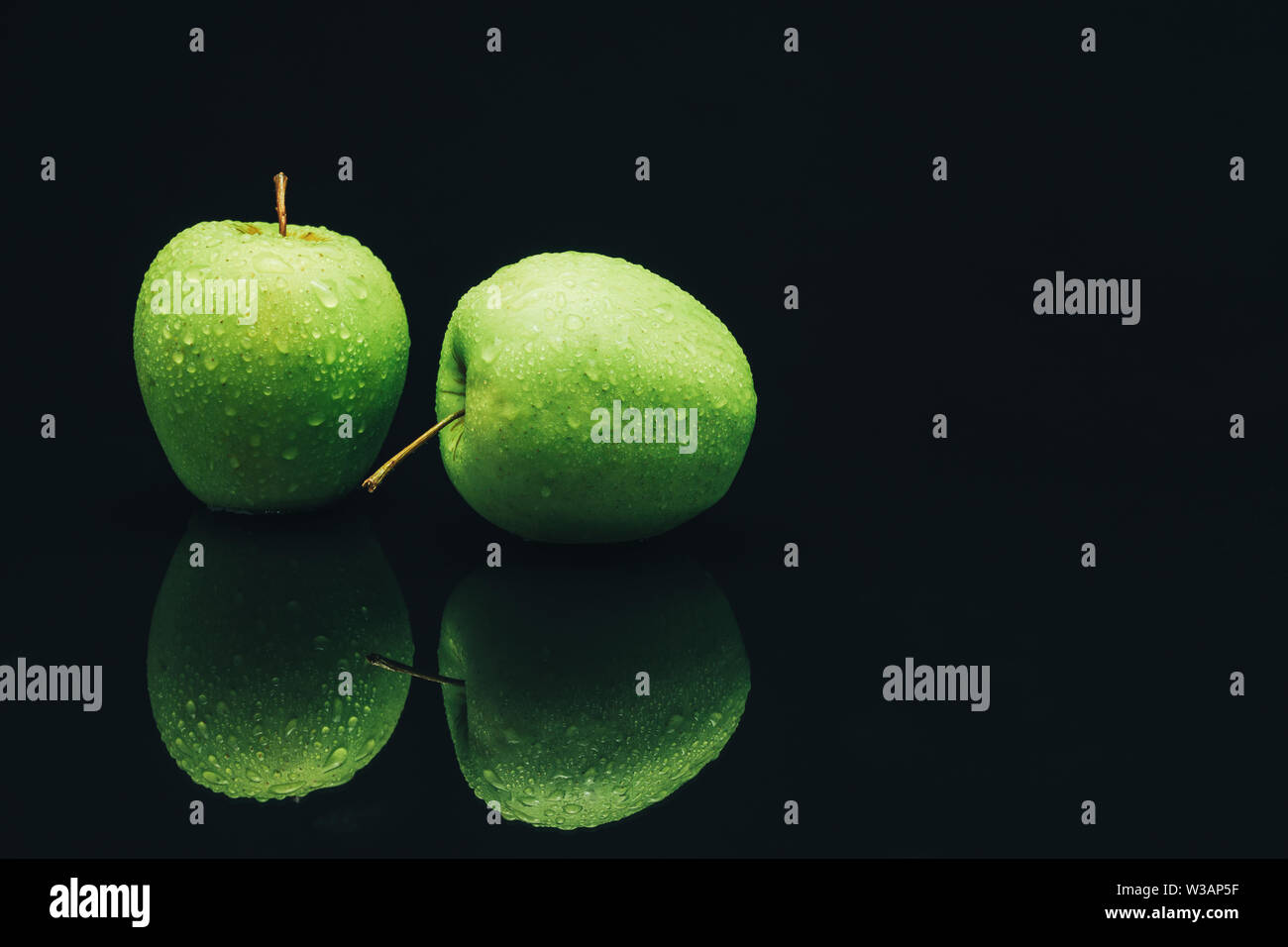 Two green apples on a black glass table background Stock Photo - Alamy