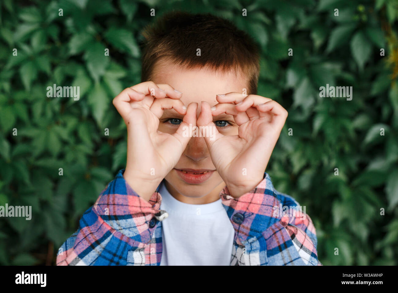 Little boy making OK gesture and looking through hand at camera outdoor ...