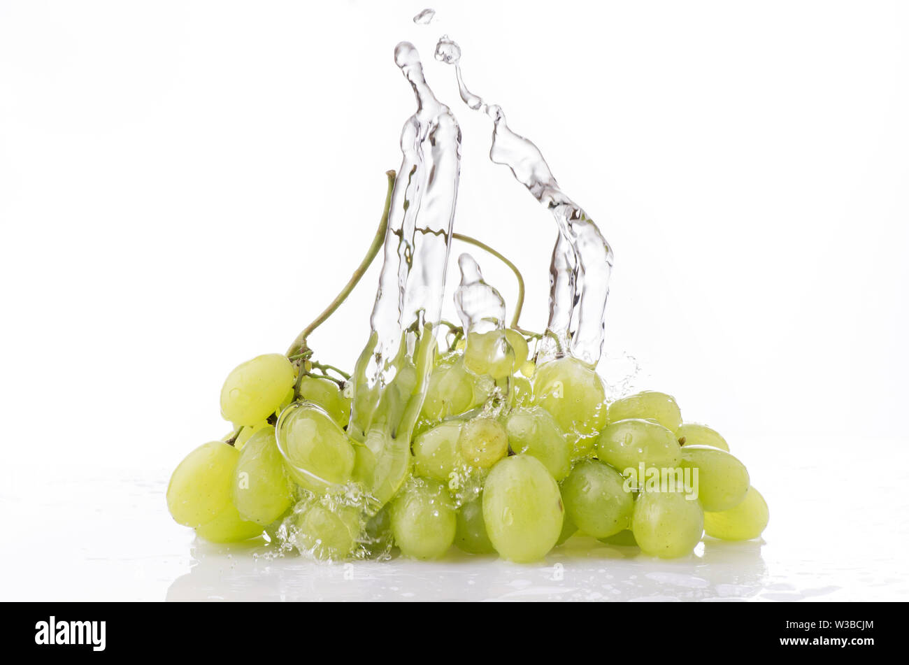 a wave of clear water falls on a cluster of white grapes on a white ...