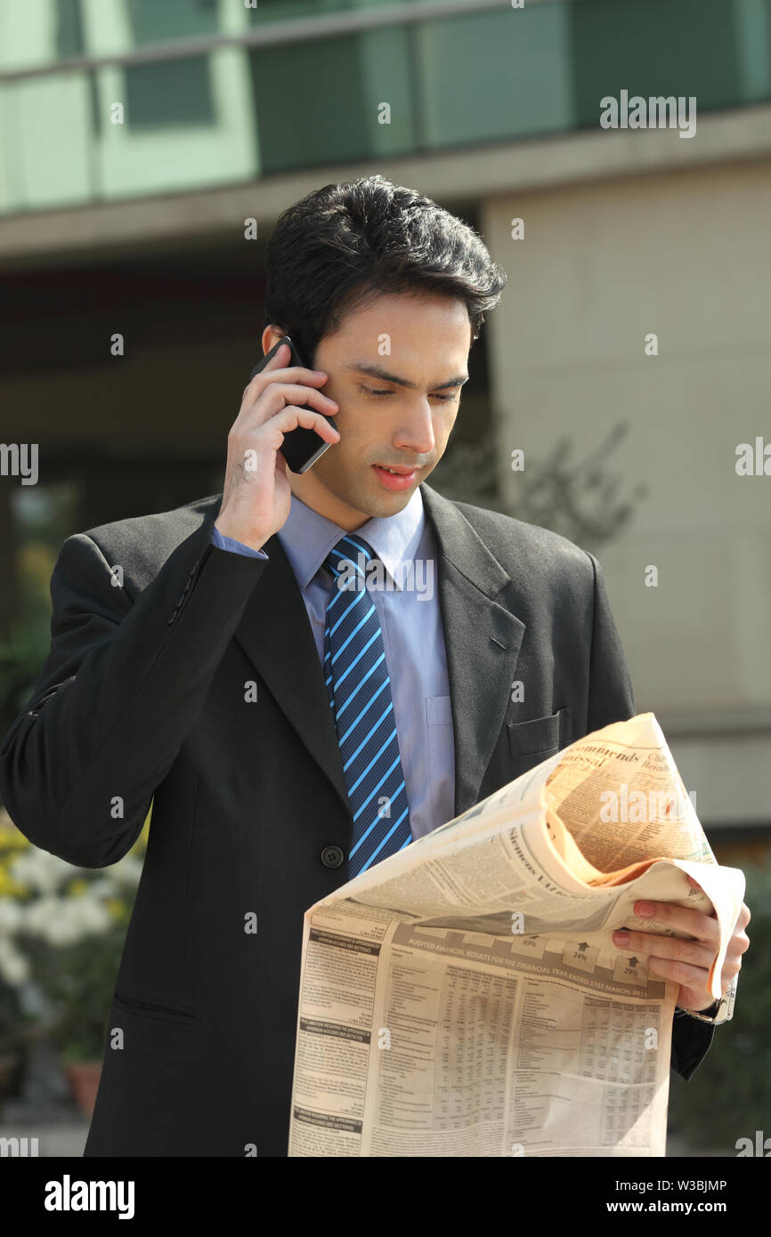 Businessman reading a newspaper and talking on a mobile phone Stock ...