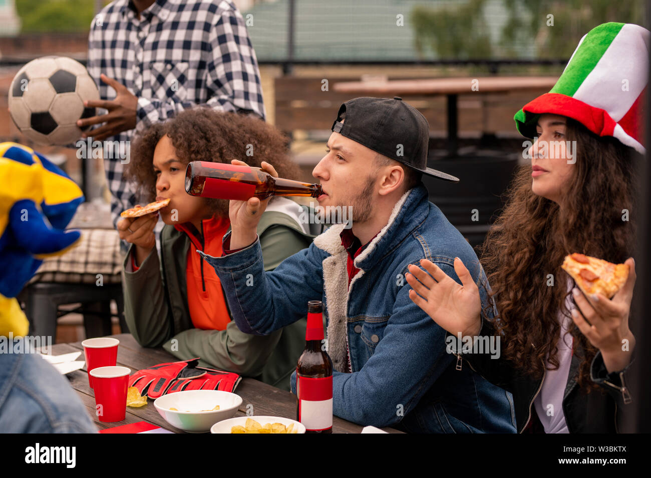 Football fans drinking beer and eating pizza while watching play of ...