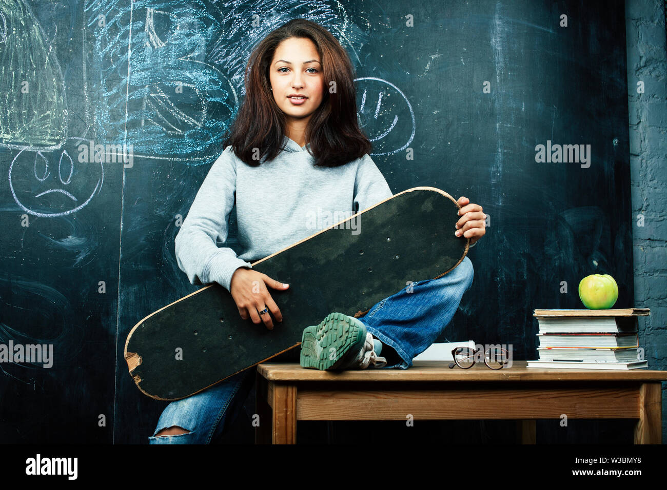 young cute teenage girl in classroom at blackboard seating on table ...