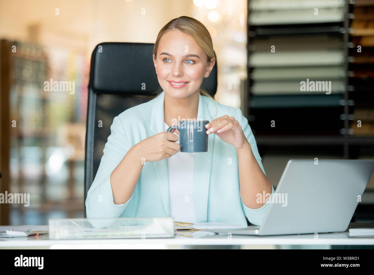 Young restful businesswoman with drink sitting by workplace Stock Photo ...