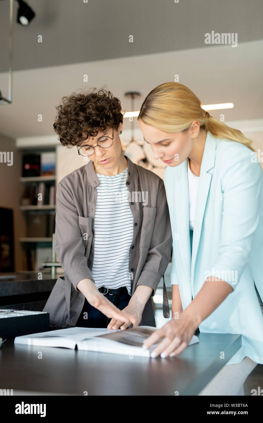 Young brunette woman explaining her colleague sketch or picture in book ...