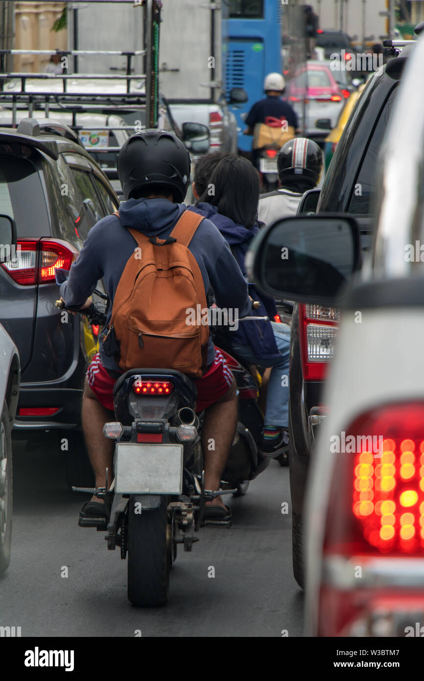 A motorbikes ride on the street in a gap between standing cars. Traffic ...