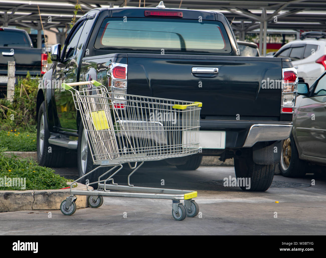 An empty shopping cart stands in a shopping mall parking lot with cars ...