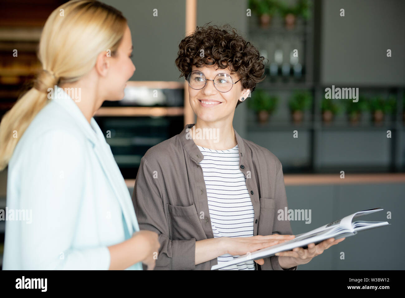 Happy young designer with catalogue listening to client preferences ...