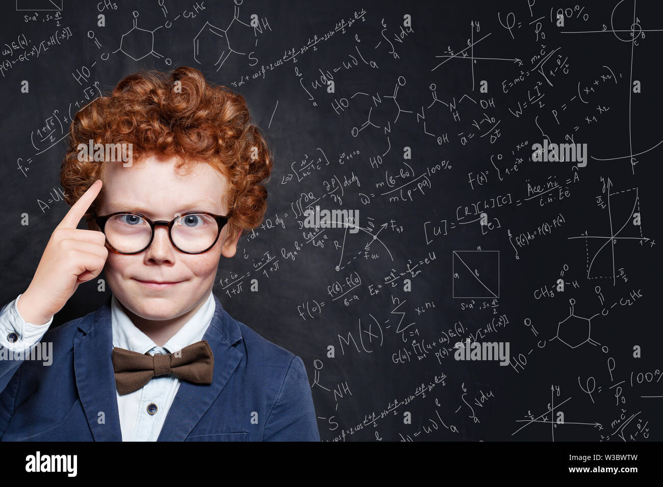 funny-redhead-smart-kid-boy-in-classroom-on-chalkboard-background-with-science-formulas-back-to