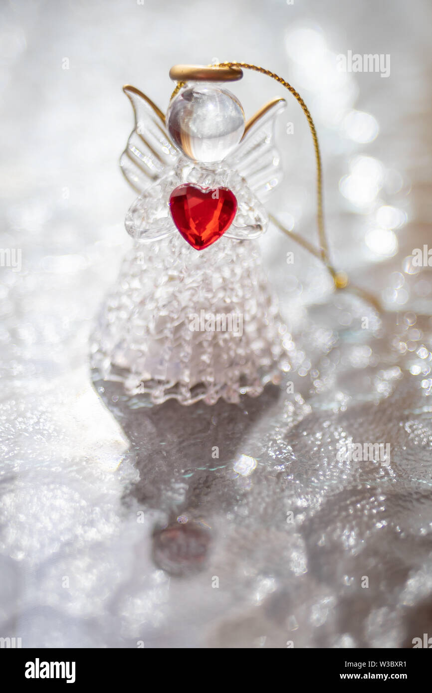 Small glass angel with a red heart in hands stands on a shiny glass ...
