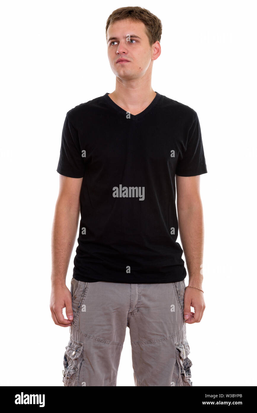 Studio shot of young man standing and thinking while looking at ...