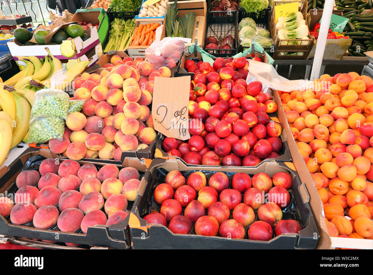 greengrocer stand at market and boxes of ripe peaches with price tag ...