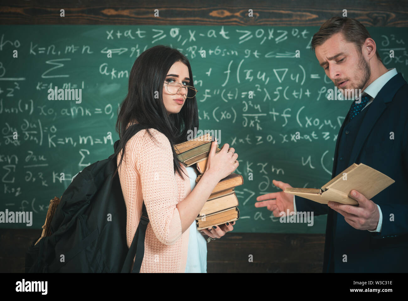 Young brunette in pink cardigan wearing glasses holding heap of books ...