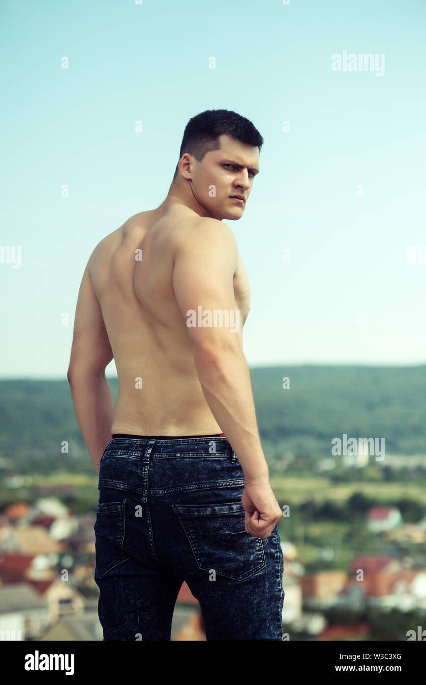 Bodybuilder with fit torso back in jeans. Man athlete on mountain on ...