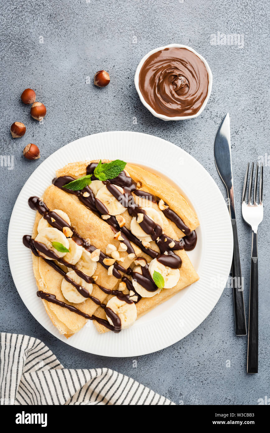 Crepes with chocolate sauce, banana and nuts on white plate. Table top ...