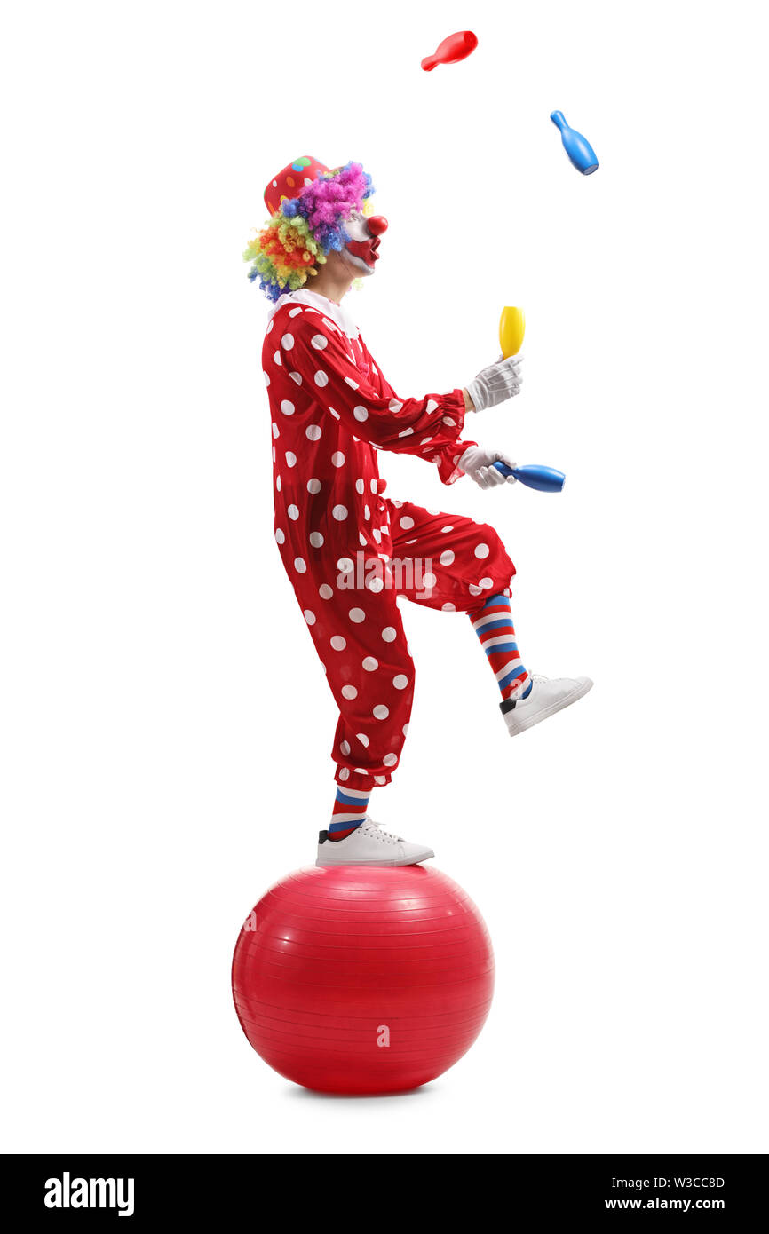 Full length shot of a clown juggling and standing on a ball isolated on ...