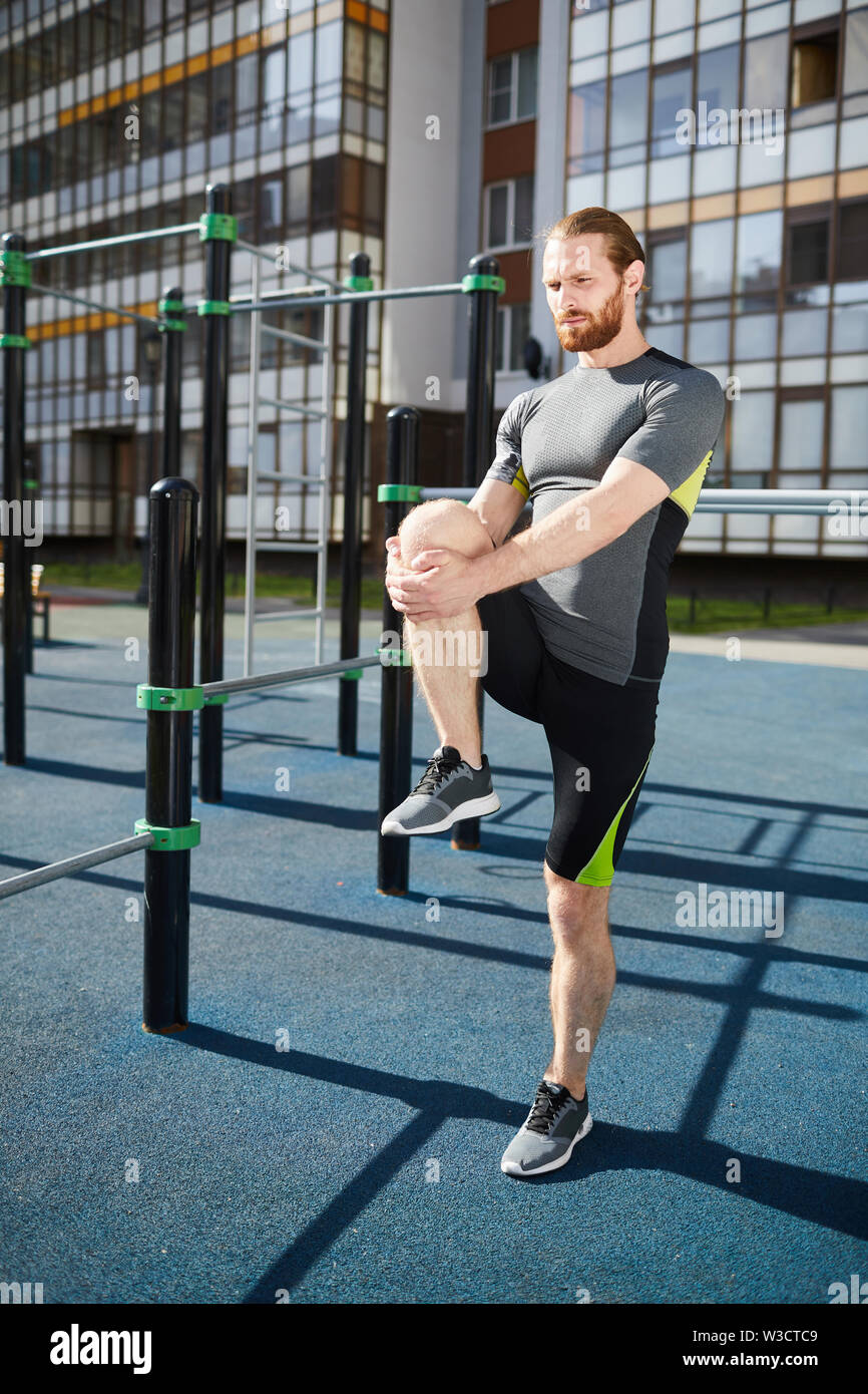 Serious fit young bearded man in tight clothing standing on one leg and ...