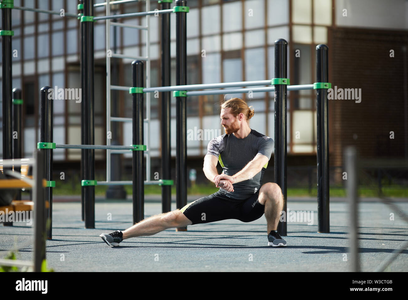 Serious slim young man in tight clothing practicing adductor stretch ...