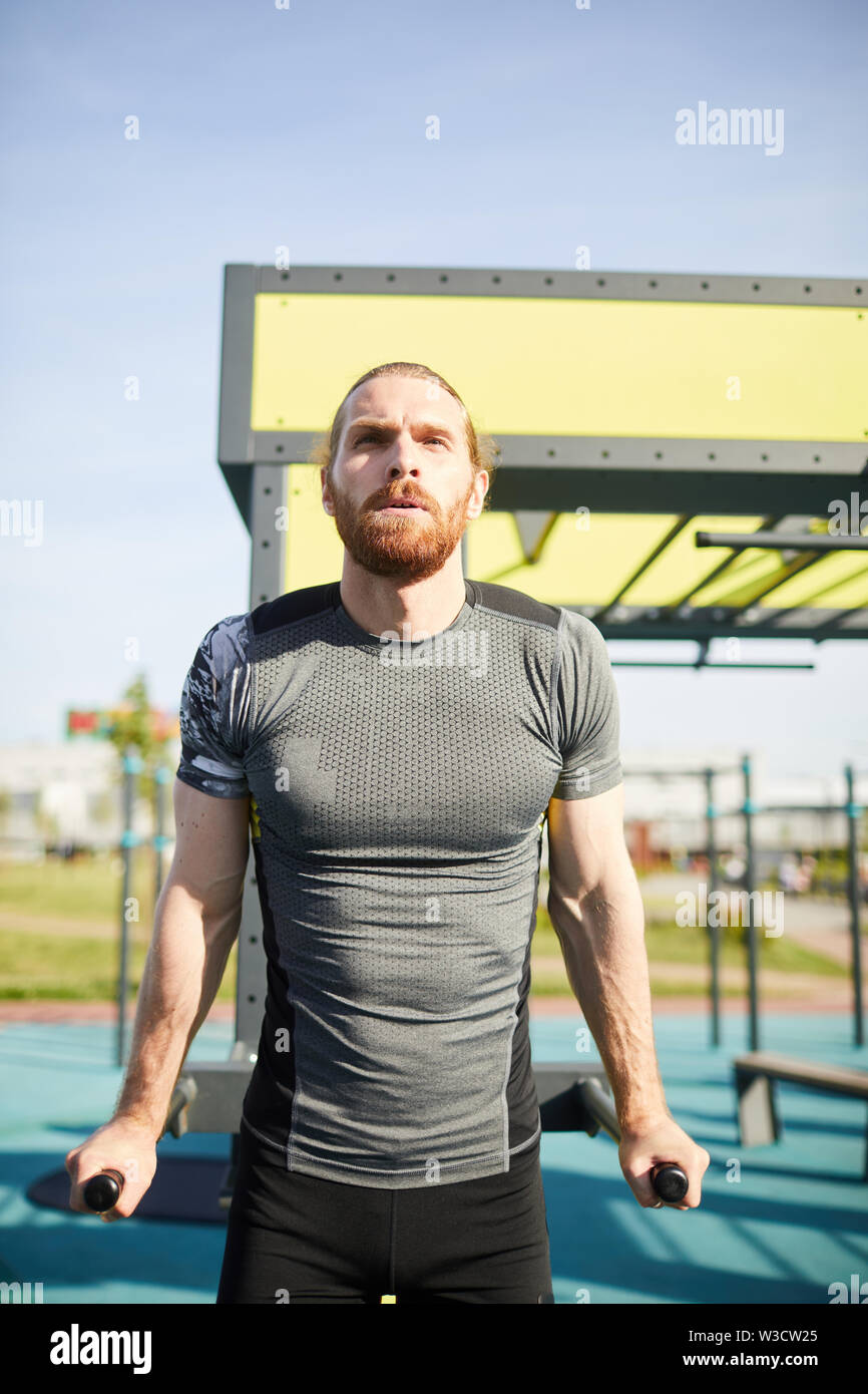 Concentrated tenacious man in sportswear exhaling while doing pull-ups ...