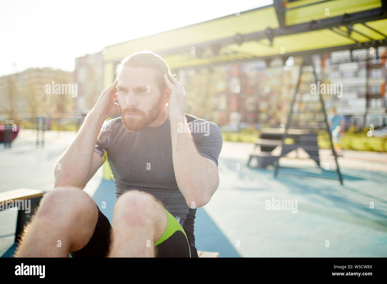 Serious fit young bearded man in tight clothing doing crunches exercise ...
