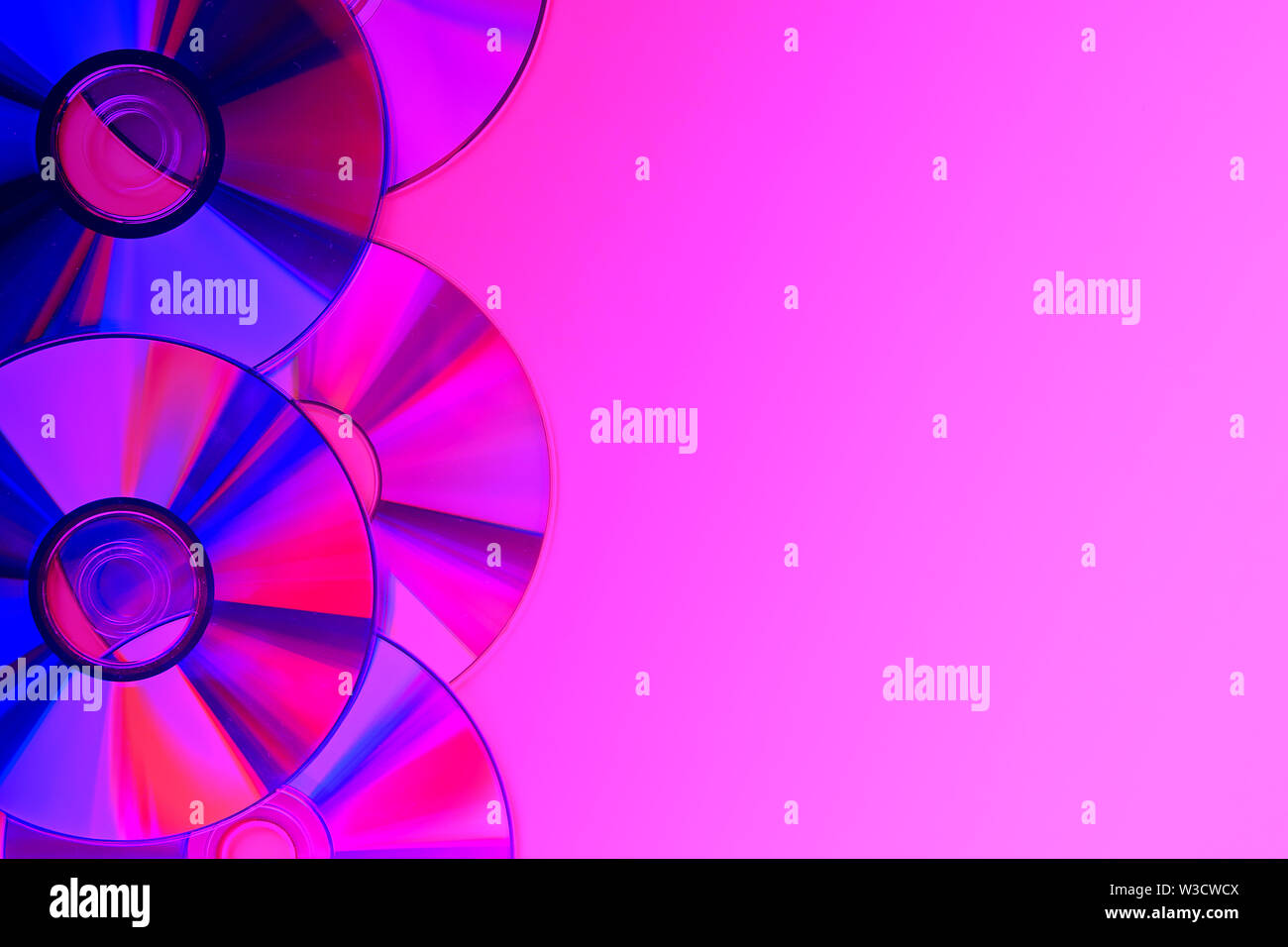 Piles of old and dirty CDs,DVD on pink violet purple neon background ...