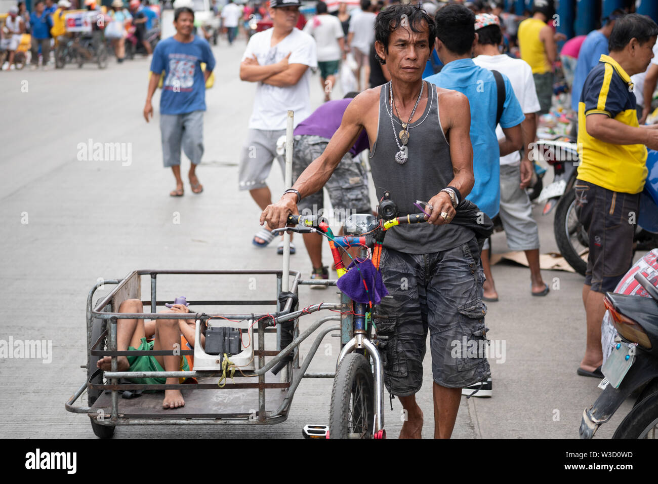 A man pushes a cart attached to a bike with a small child lying inside ...