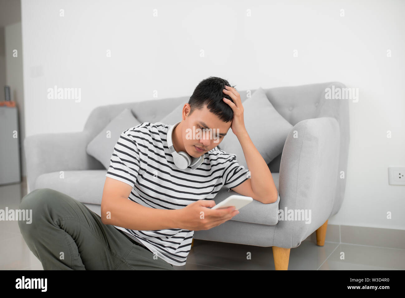Single sad man checking mobile phone sitting on the floor in the living ...
