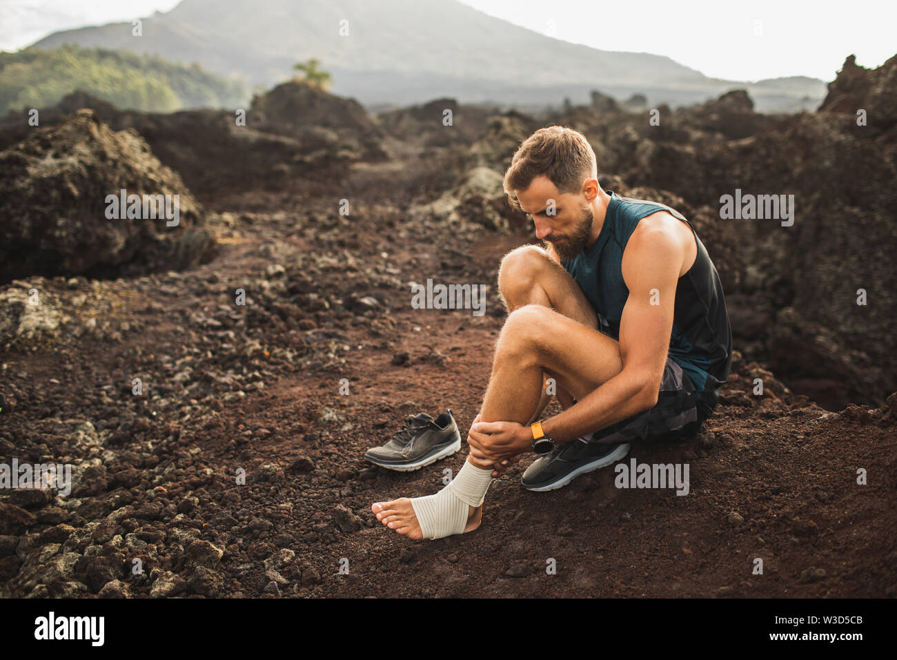 Male runner bandaging injured ankle. Injury leg while running outdoors ...