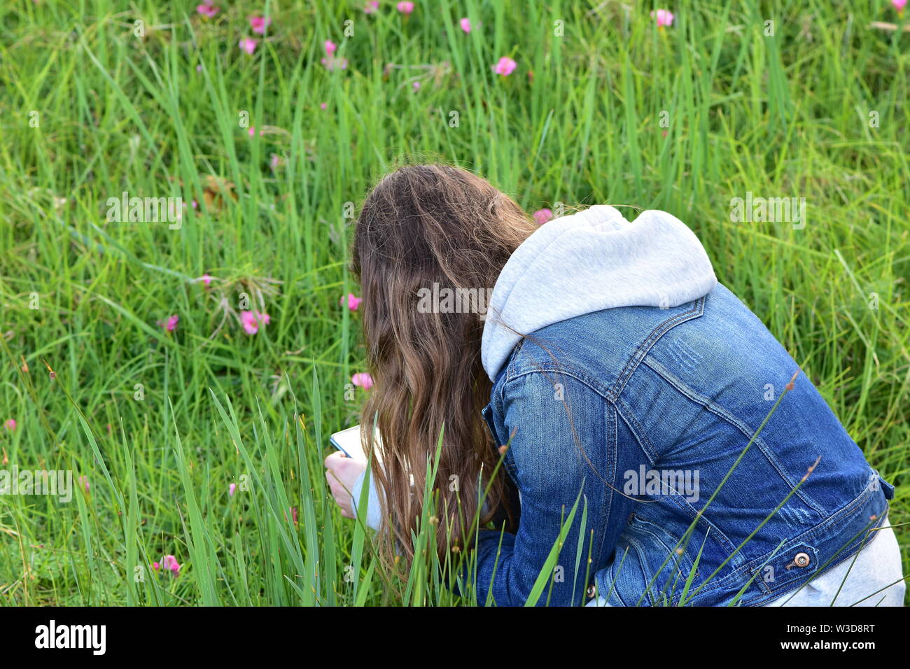 Girl with long hair wearing denim jacket crouching in tall grass among ...