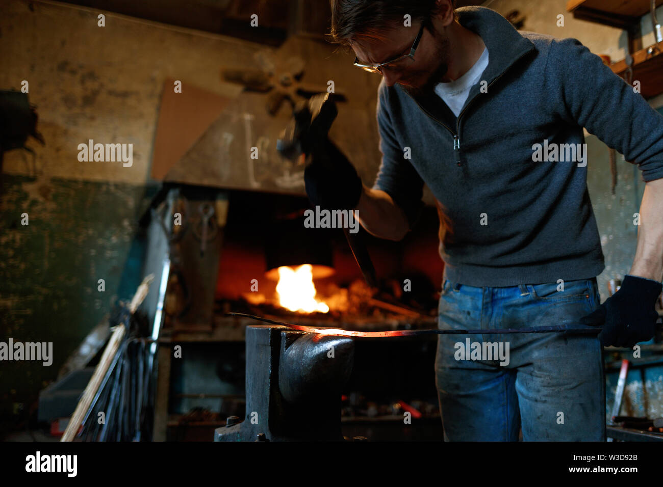 Blacksmith forging red-hot metal with hammer. Over furnace background ...