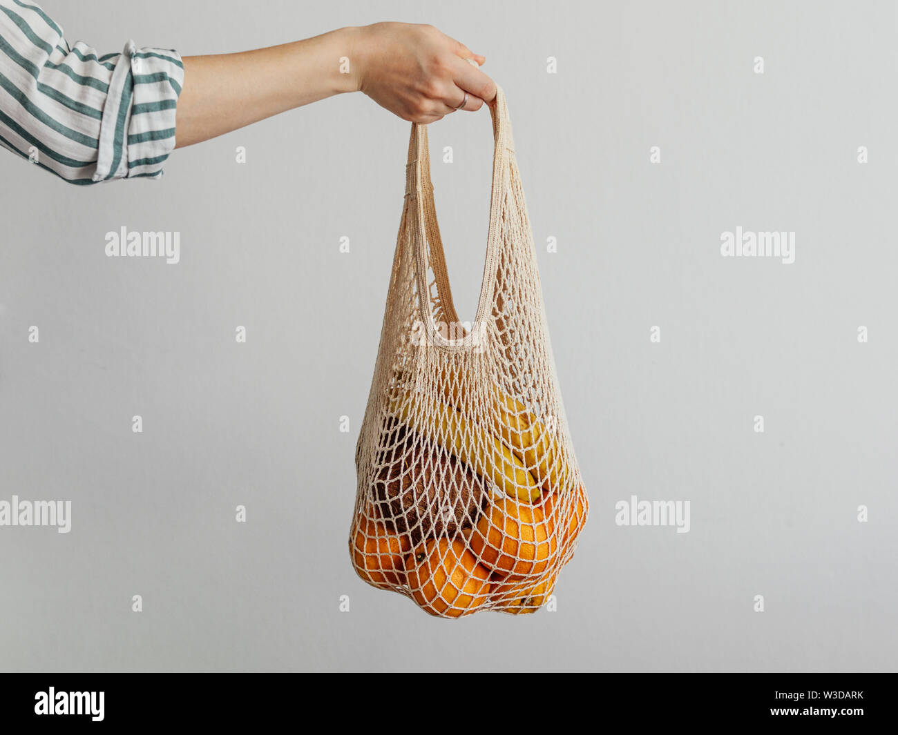Mesh bag with fruits in female hand. Stylish young woman hand hold mesh ...