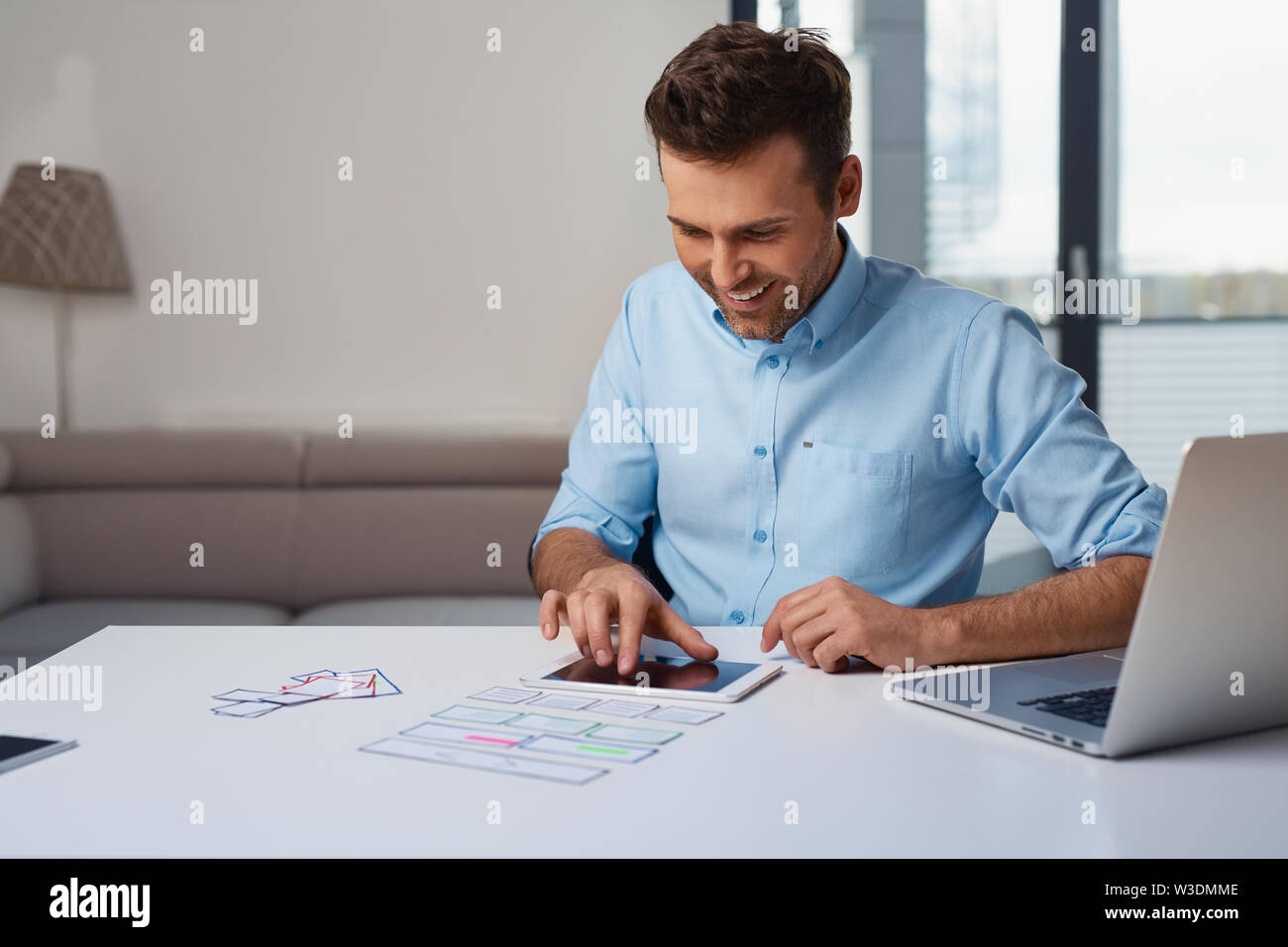Smiling web developer prototyping in home office with laptop and tablet ...