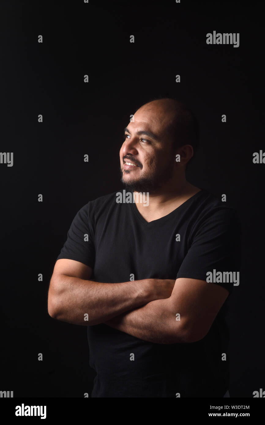 portrait of profile of a latin american man arms crossed on black ...