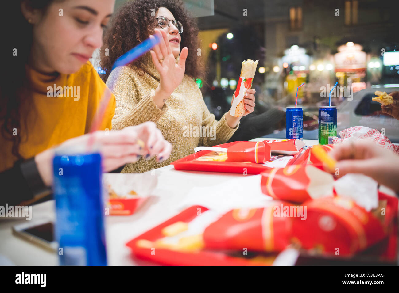 young curly woman eating in fast food with friends - hungry, break ...