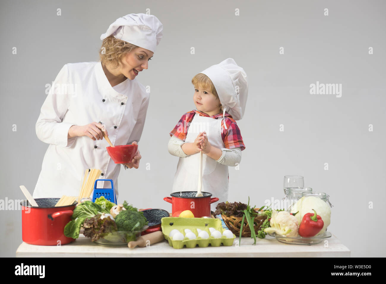 Mother teaches son to cook on light background. Mom and kid with busy ...