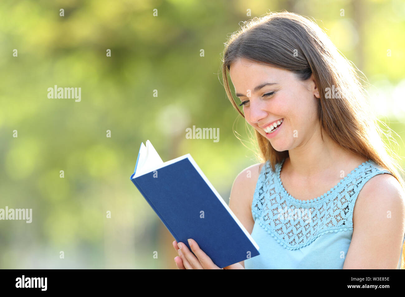 Happy woman reading a blank paper book on green background in a park ...