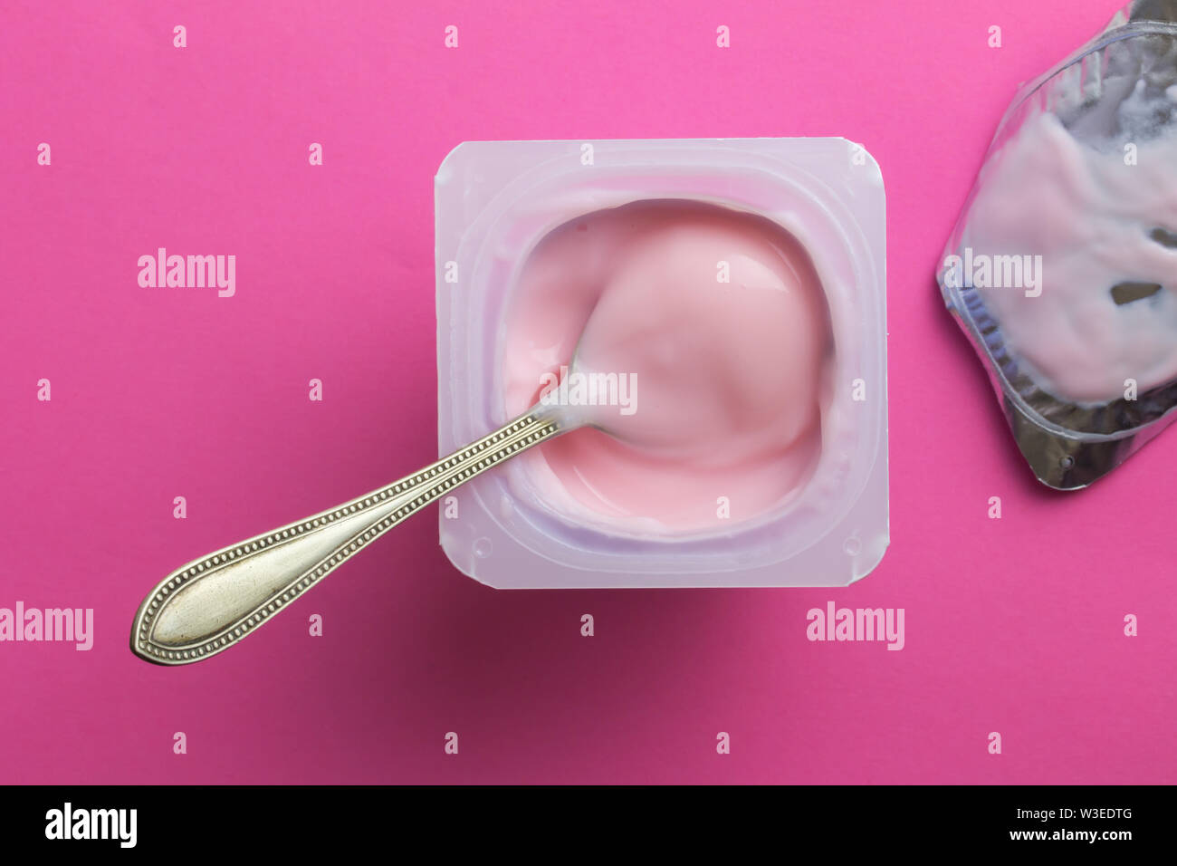 Strawberry pink yogurt in plastic cup with spoon and foil lid isolated ...