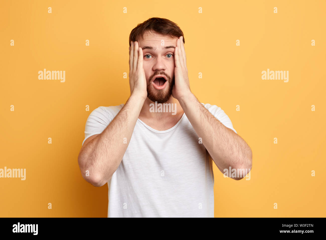 emotional scared handsome man with hands on cheek and wide open mouth ...