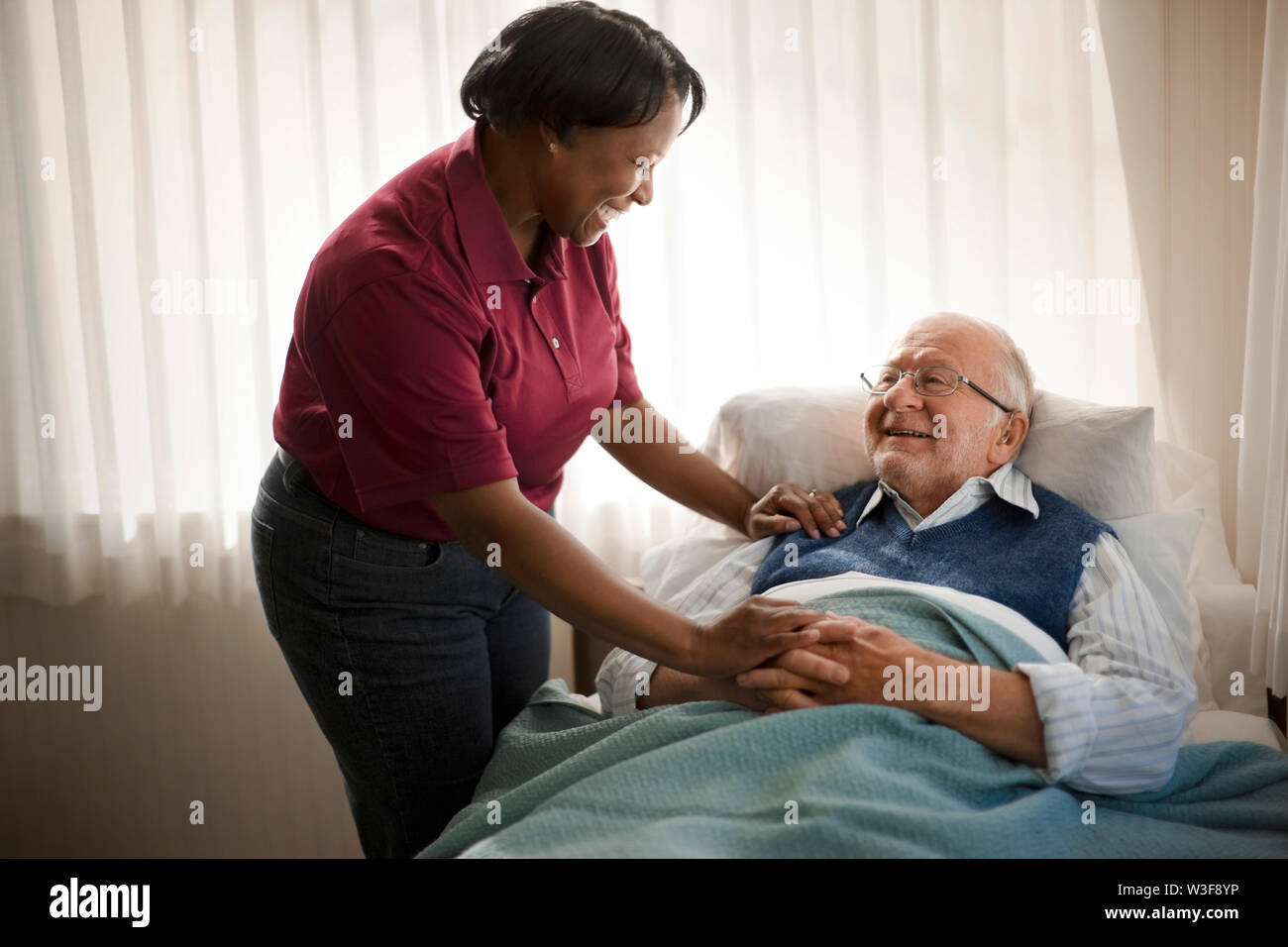 Happy female nurse comforting an elderly patient at his bedside Stock ...