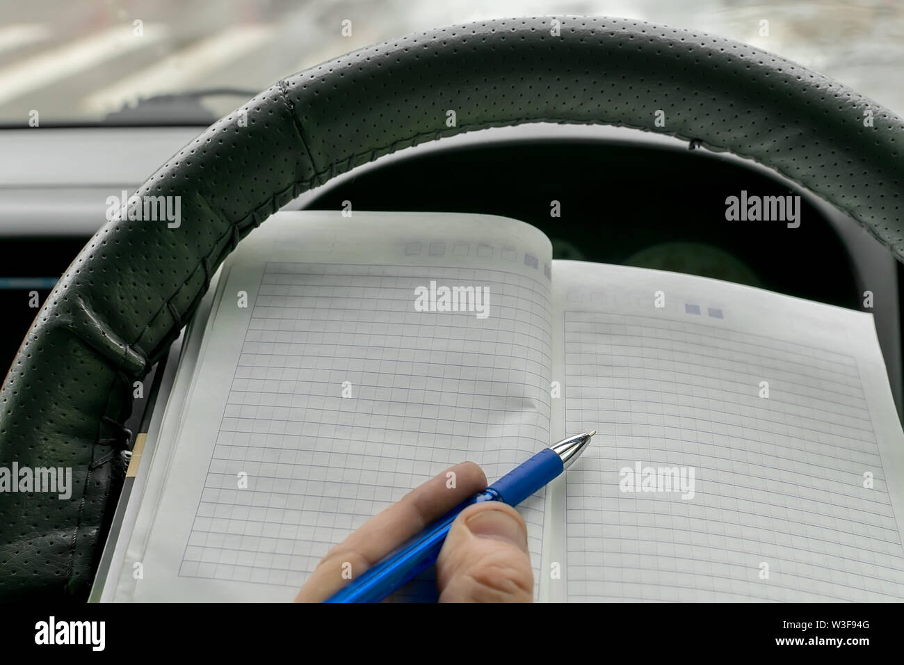 the hand of the car driver behind the wheel holds a paper notebook and ...