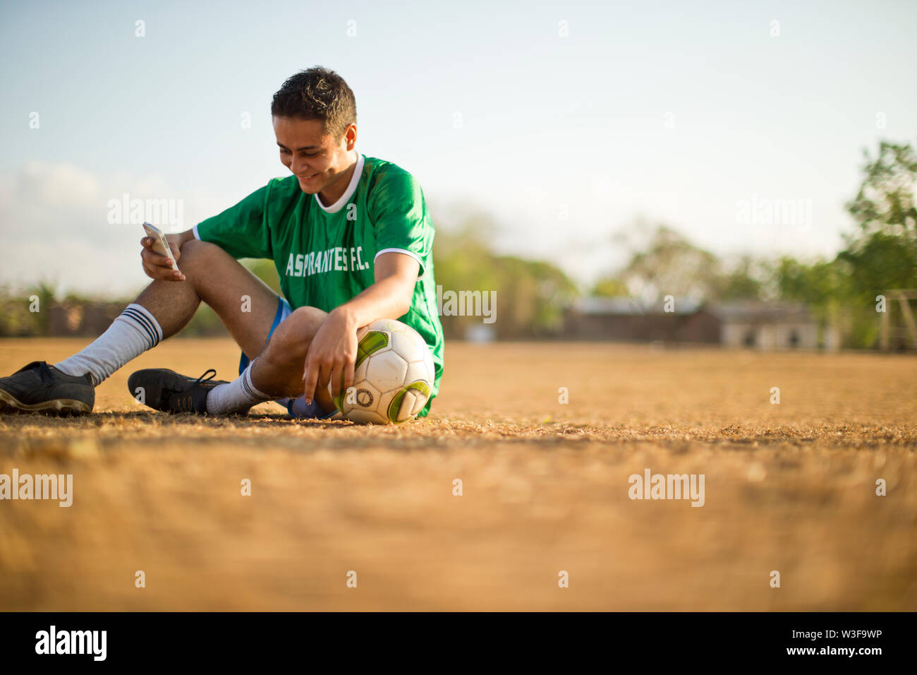 Laughing young soccer player sending a text message while sitting on a ...