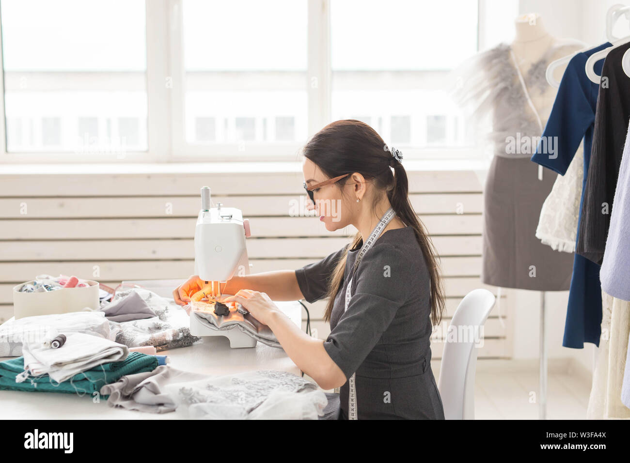 People and fashion concept - Young dressmaker woman sews clothes on ...