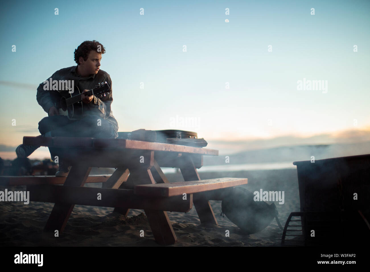 Guitar player on beach at dawn with smoke from dying campfire Stock ...