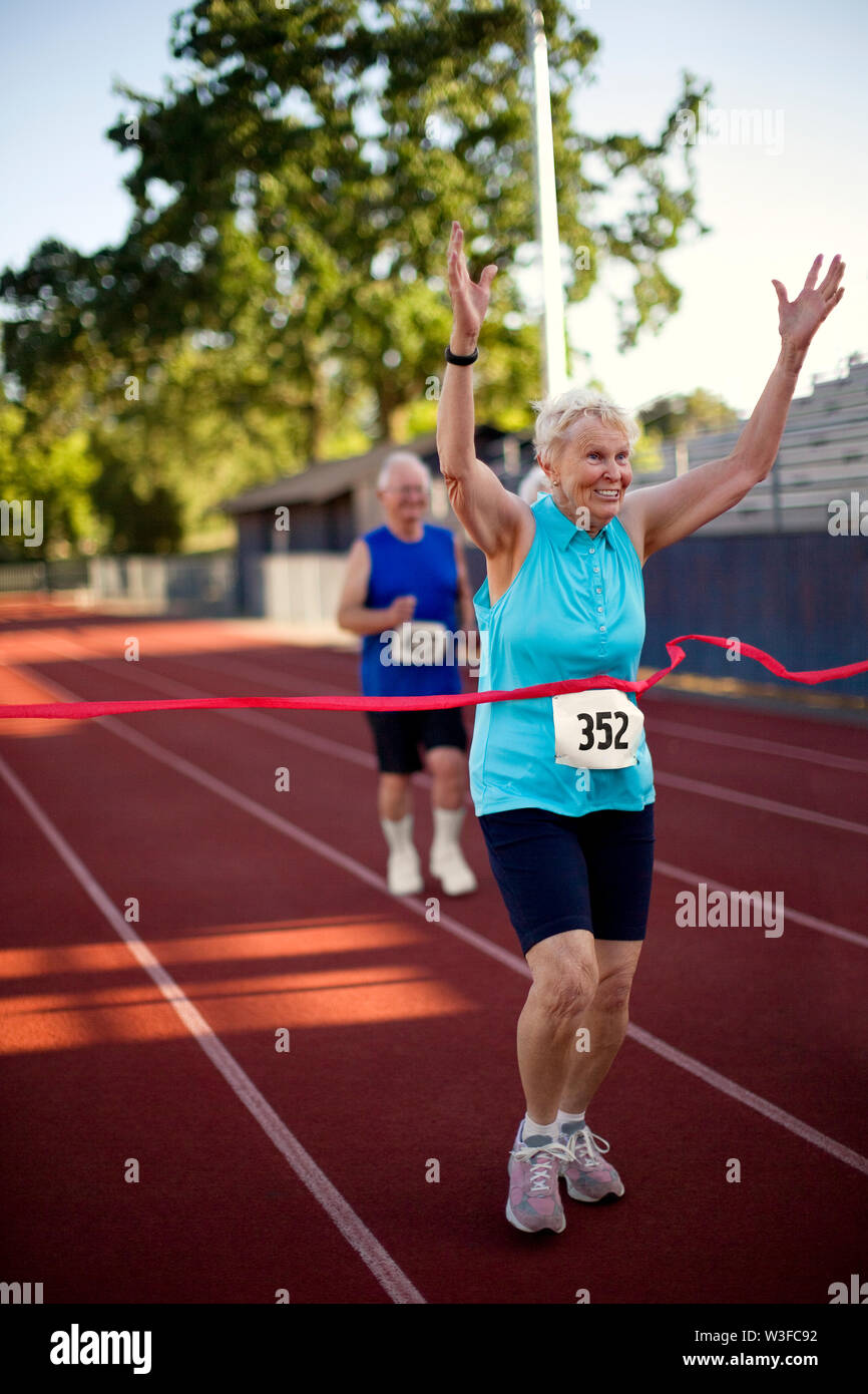 Senior woman raising her arms in triumph as she crosses the finish line ...