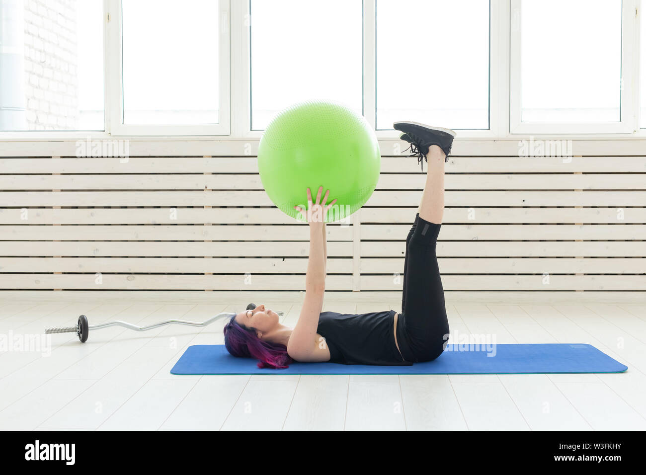 Young slim girl does exercise and stretching on a green fitball In the ...