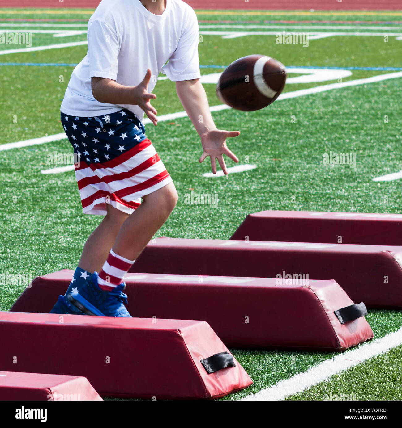 A young boy is at summer football camp catching a football while ...