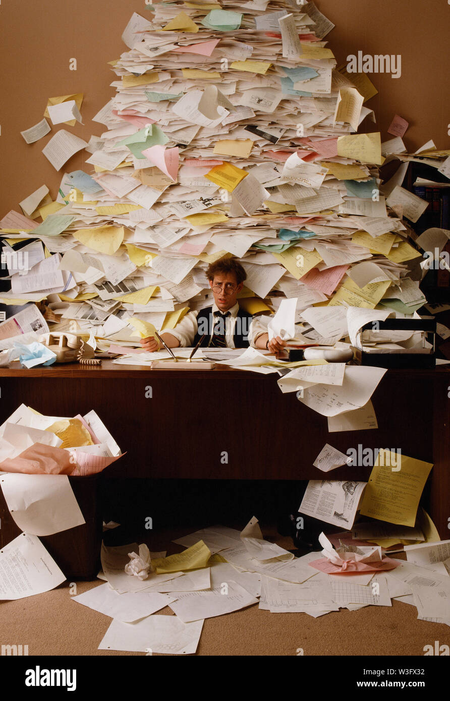 Guy at desk under mounds of paper Stock Photo - Alamy